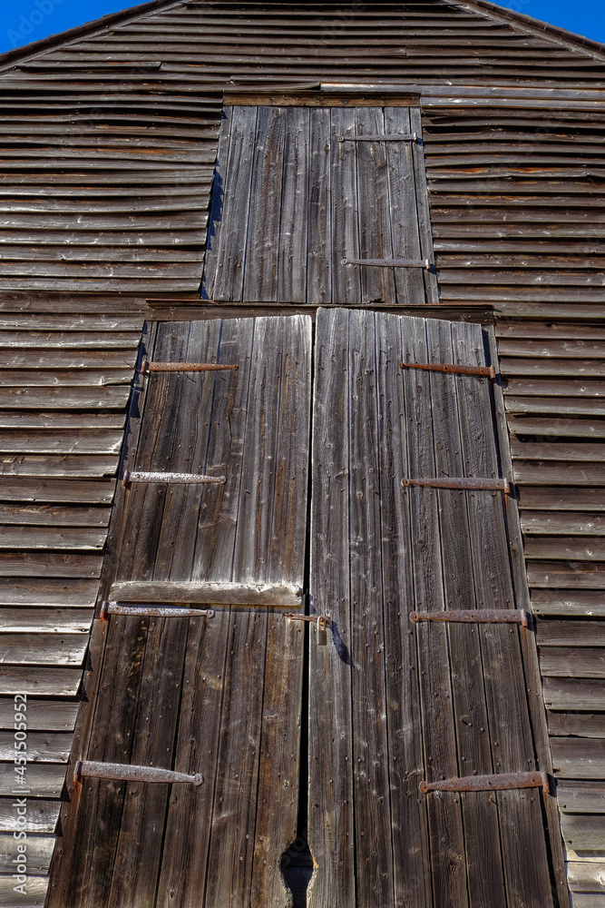 The large weather beaten wood doors of a large barn with rusted hinges ...