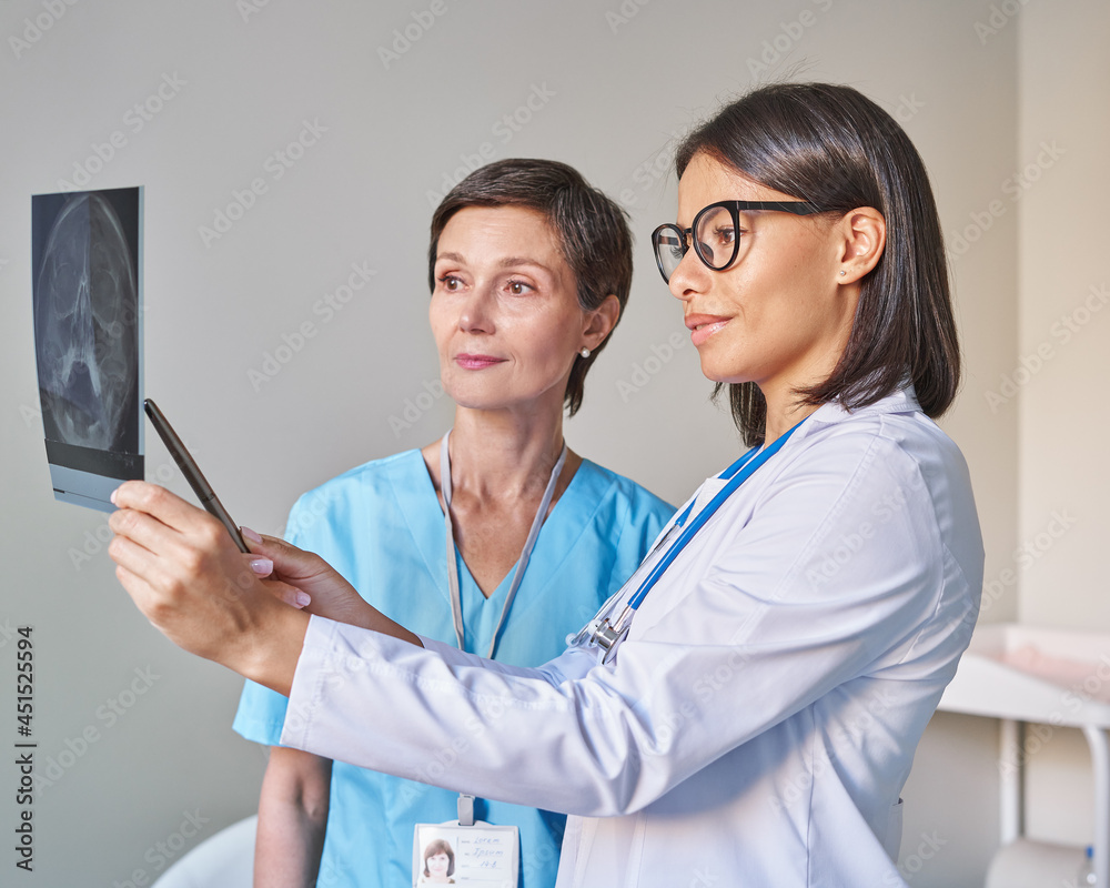Two women doctors in uniform looking at brain tomography and discussing ...