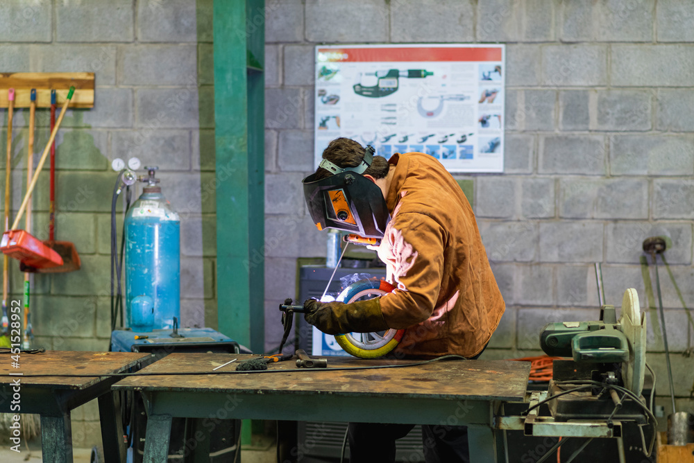Hombre soldando en un taller con protección para el rostro y sus cuerpo ...