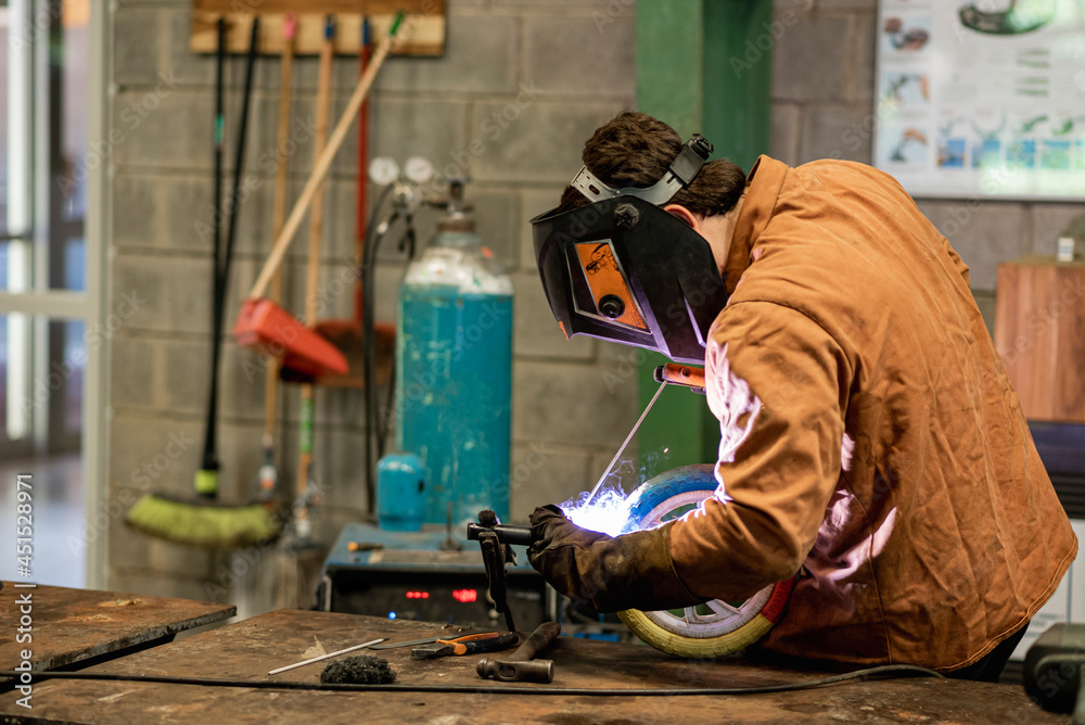Hombre soldando en un taller con protección para el rostro y sus cuerpo ...