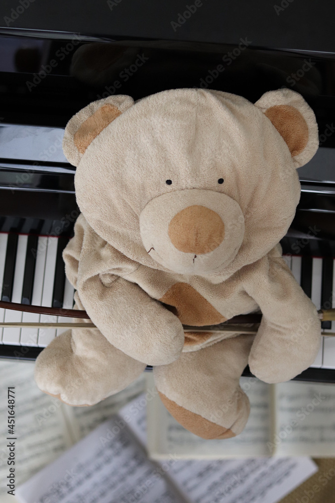 Teddy bear sitting and smiling on a piano holding a bow and music ...