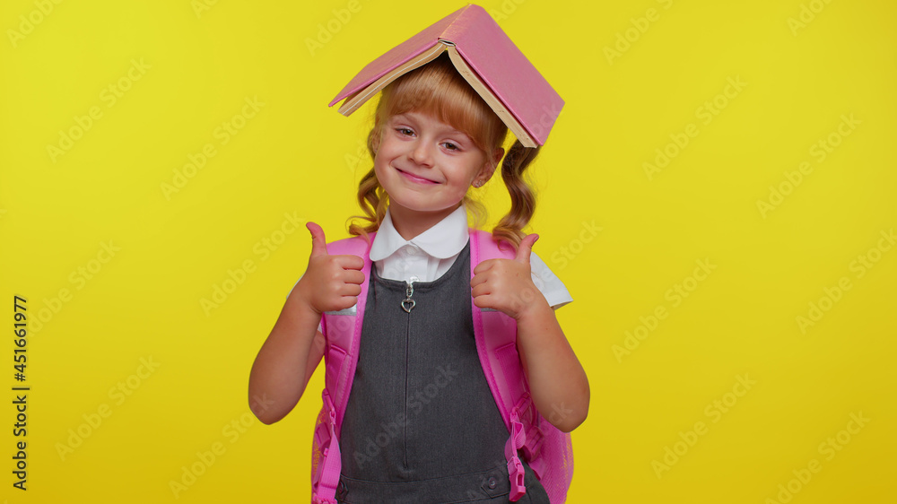 Smiling cute schoolgirl wears backpack, reading book, making playful ...