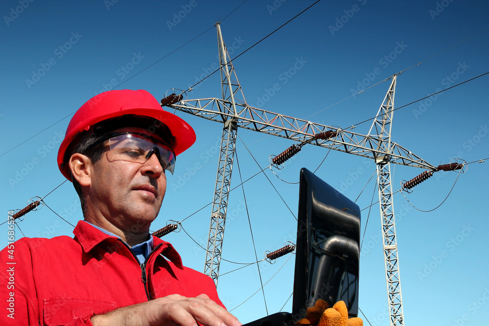 Electrical engineer with red hard hat using laptop outdoors in front of ...