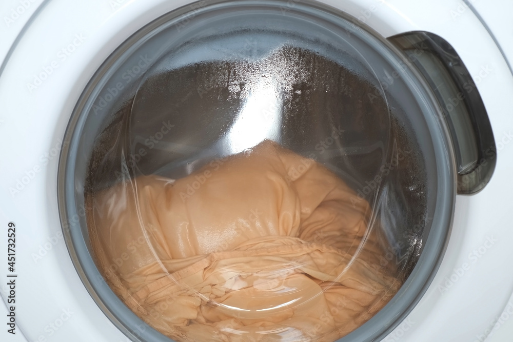 Washing machine with beige bed linen inside is working, laundry at home ...