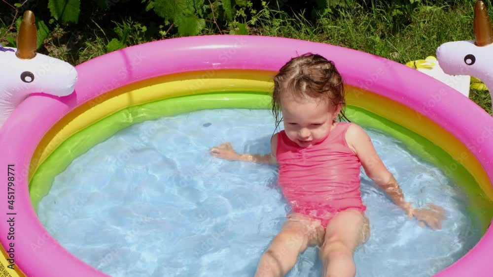 A girl in a small children's inflatable pool turns over in the water ...