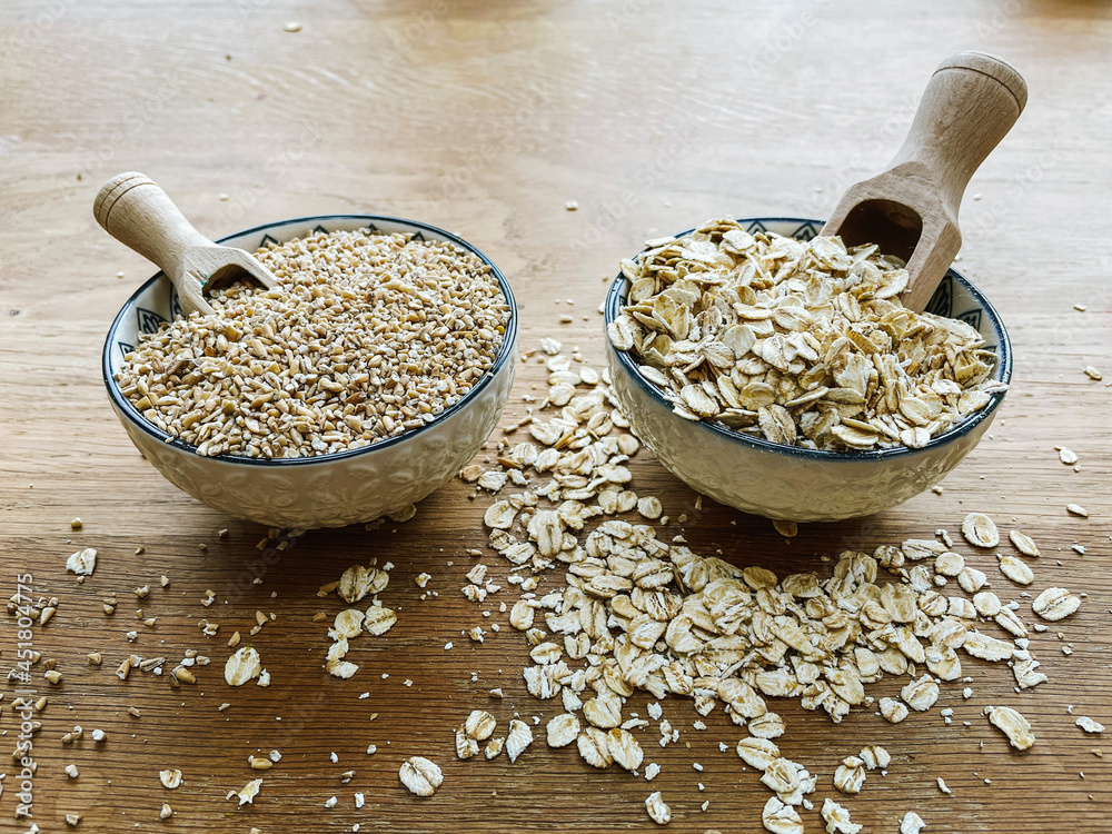 Steel cut / pinhead oats vs rolled oats in bowls with wooden scoops ...