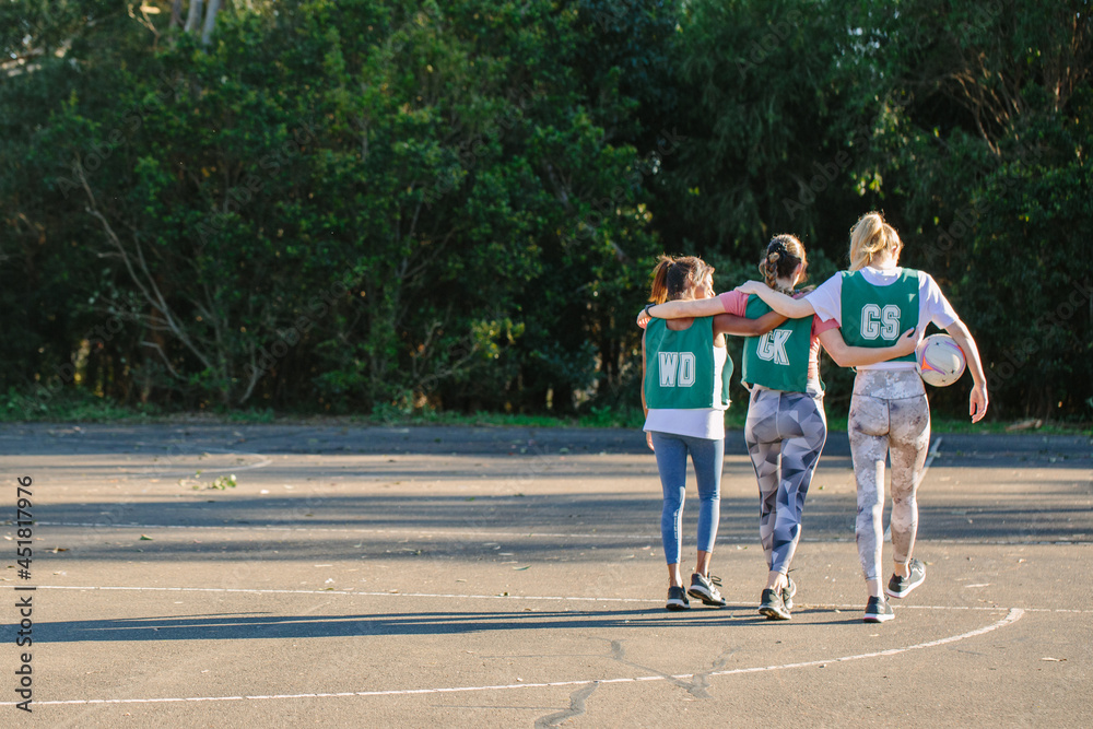 horizontal shot of three young women walking away with arms wrapped ...