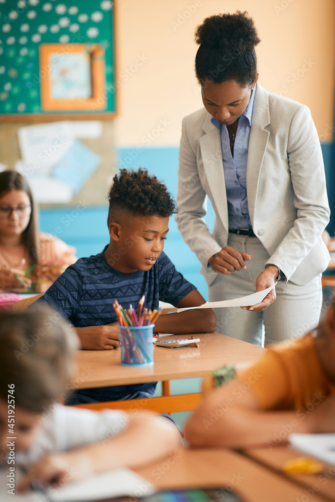 African American school teacher assists her student during class in ...