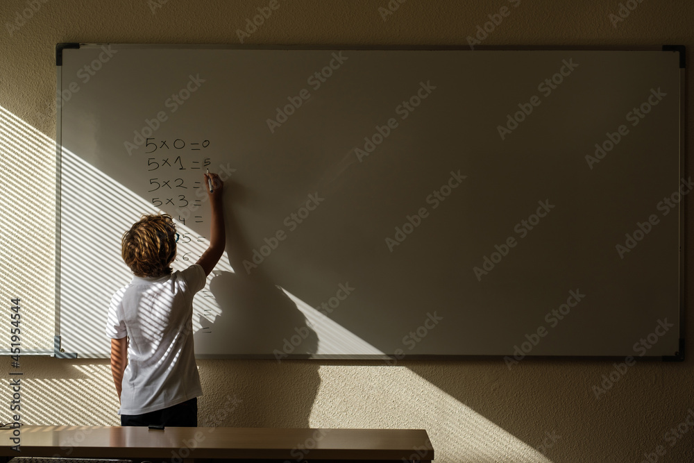 Back view of anonymous schoolboy writing multiplication table on ...