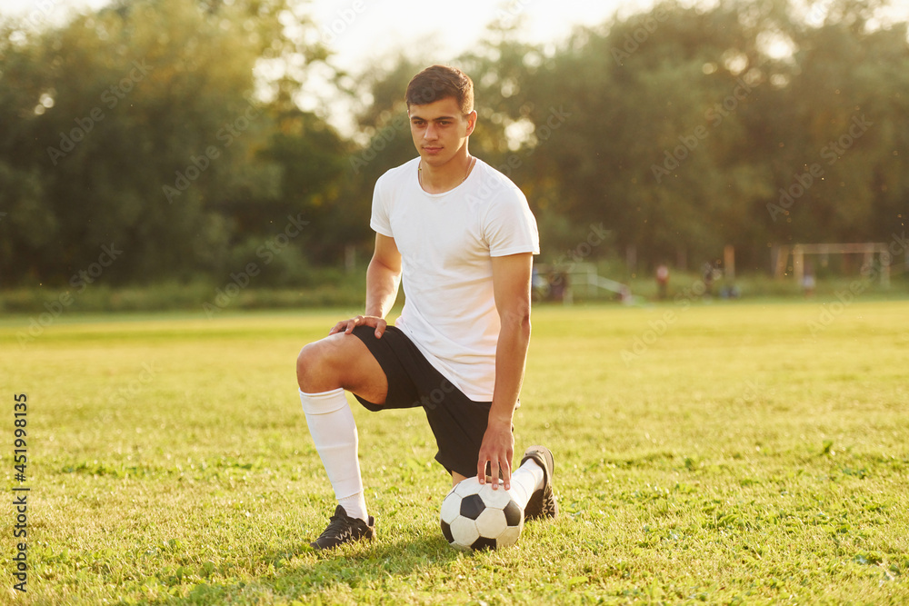 Sits on the knee with ball. Young soccer player have training on the ...