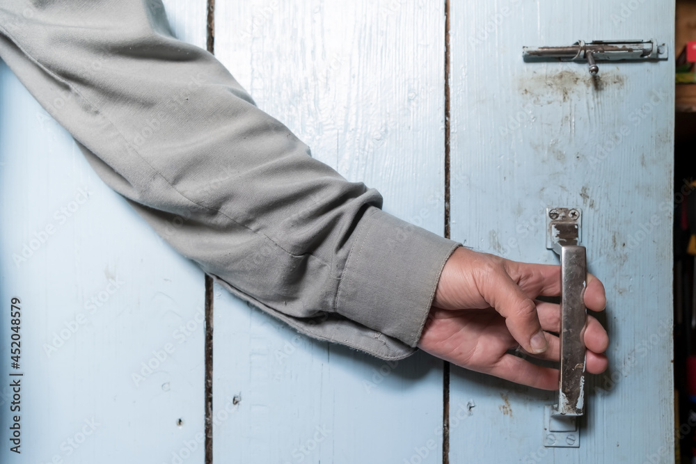 Man hand in shirt opens a wooden door with a latch, painted in blue, in ...