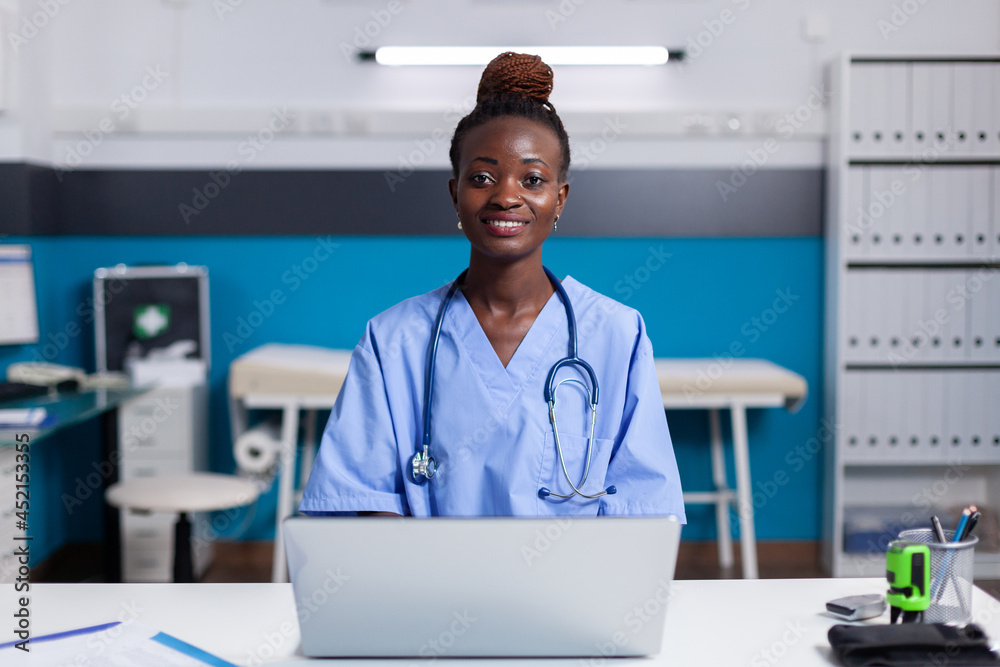 Portrait of african american nurse using laptop at white desk sitting ...