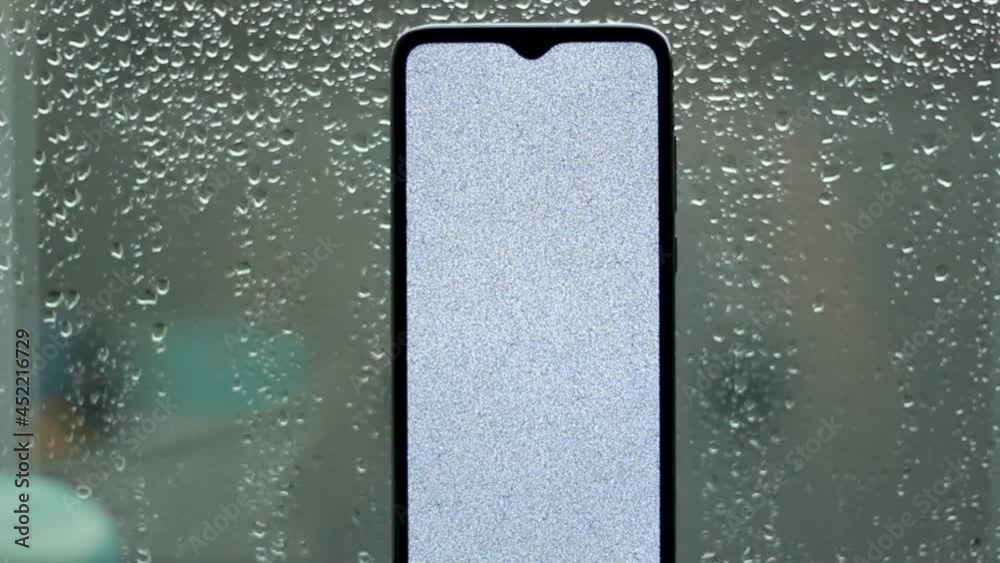 White Noise TV animation on mobile phone against glass window with dew ...