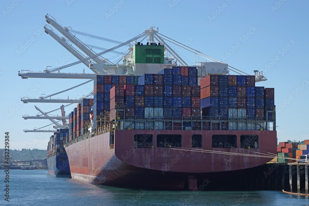 Two large, nondescript container ships are shown dock in a port next to ...