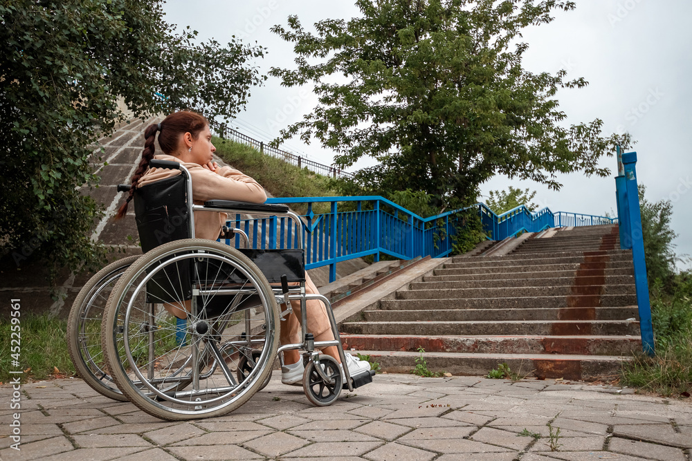 A young disabled girl sits in a wheelchair in front of the stairs. The ...