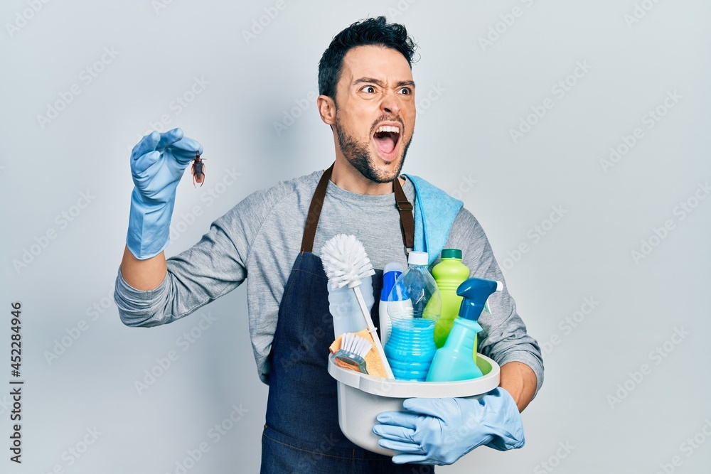 Foto de Young hispanic man holding cleaning products and cockroach ...