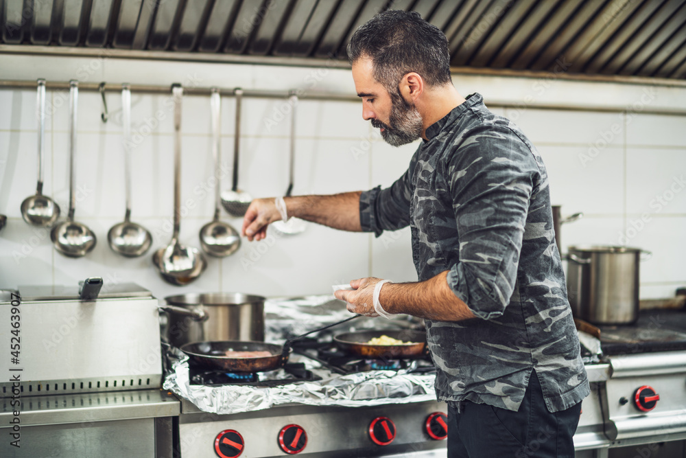 Foto de Professional cook is preparing meal in restaurant's kitchen. He ...