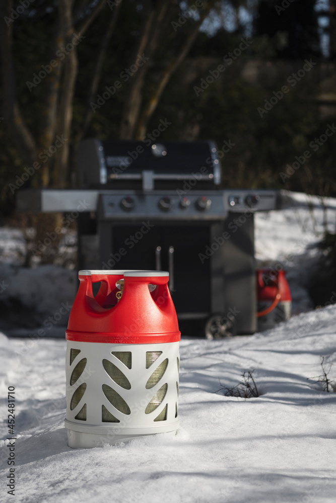 Composite gas cylinder of red and gray color and gas grill on the ...