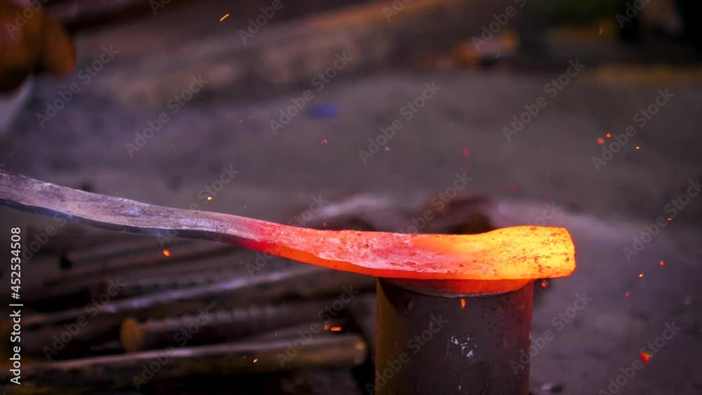 Closeup shot of man hitting red hot metal with iron hammer. Blacksmith ...