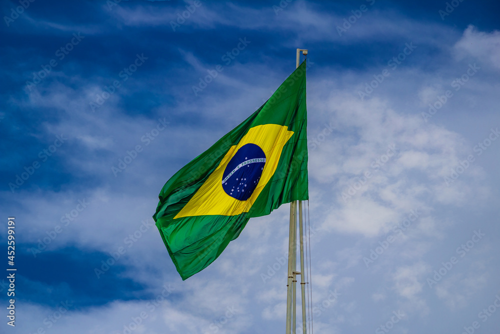 Bandeira do Brasil hasteada, tremulando ao vendo e com céu azul e ...