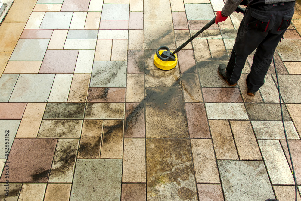 Cleaning stone slabs on patio with the high-pressure cleaner. Person ...