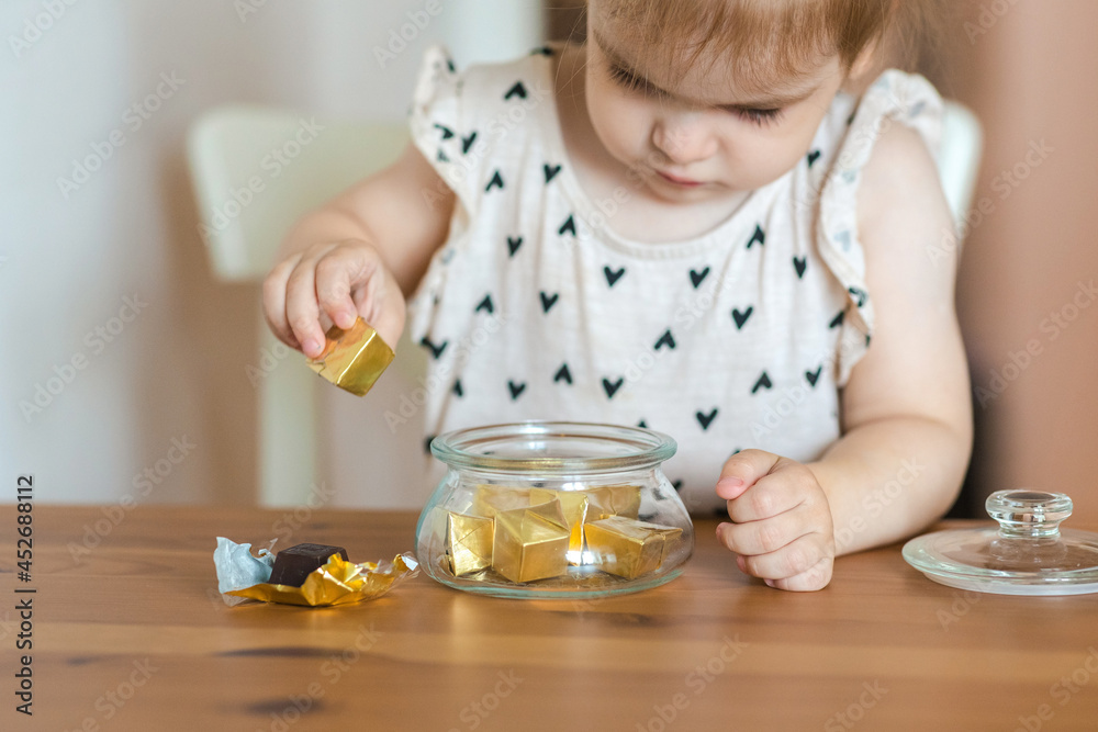 A two-year-old girl reaches for a chocolate candy from a jar. Should ...