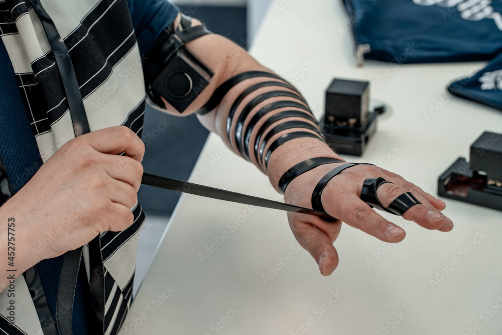 Religious adult jewish man puts black leather tefillin on his left arm ...