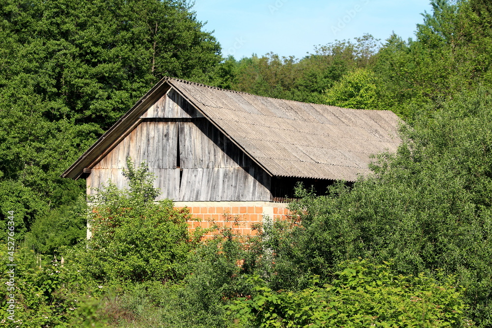 Abandoned dilapidated red building blocks and wooden boards large barn covered with old roof ...