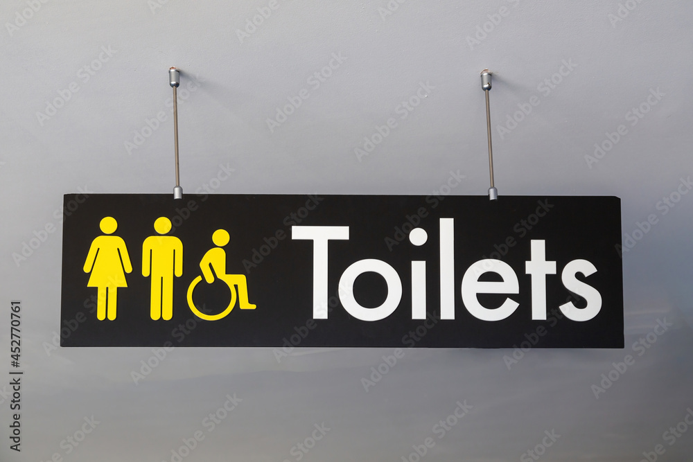 A toilets sign hanging from the ceiling pointing to the male female and ...