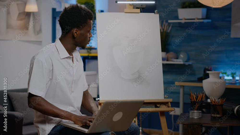 Black creative artist holding laptop computer in art studio space ...