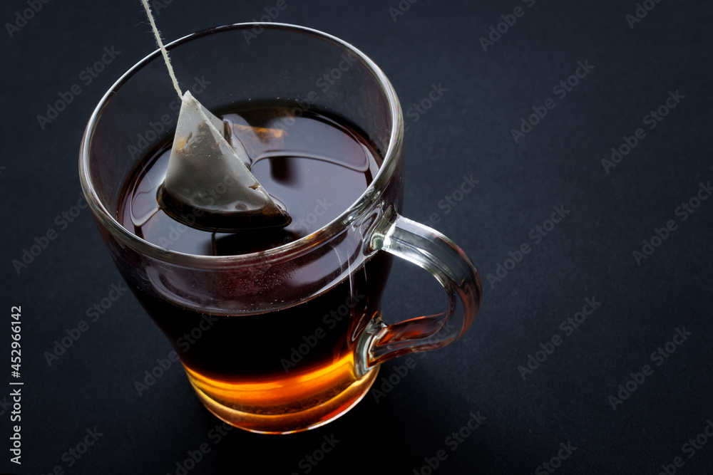 Black tea in a pyramid tea bag is brewed in hot water in a transparent ...