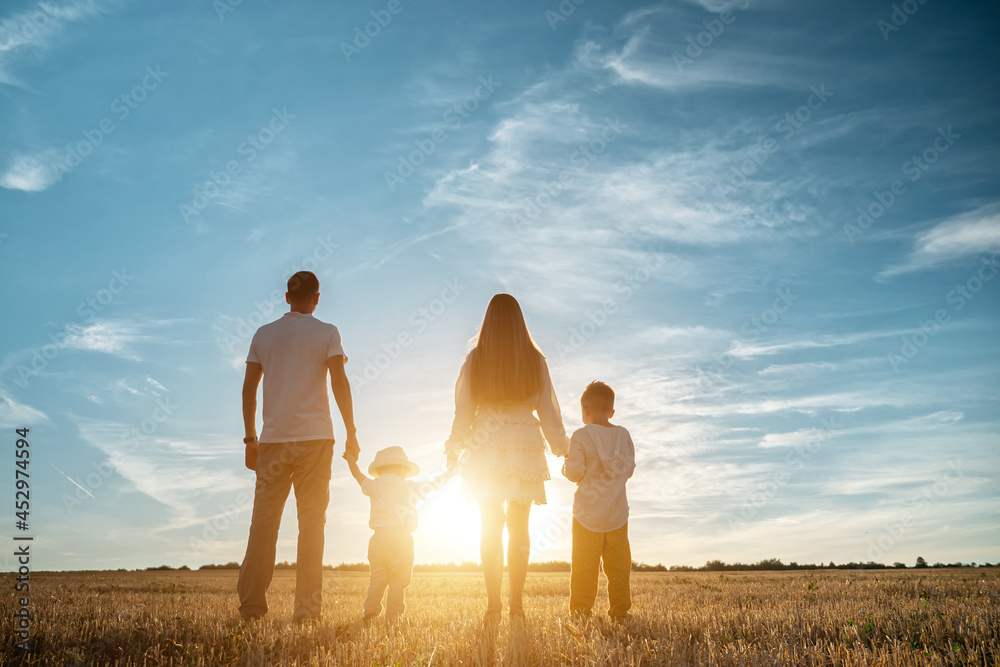 Family with children sons stands joining hands along shadowed field at ...