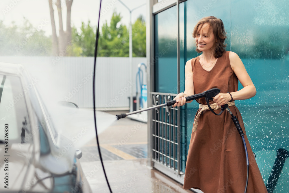 Foto de Side view young adult woman washing car with high pressure ...