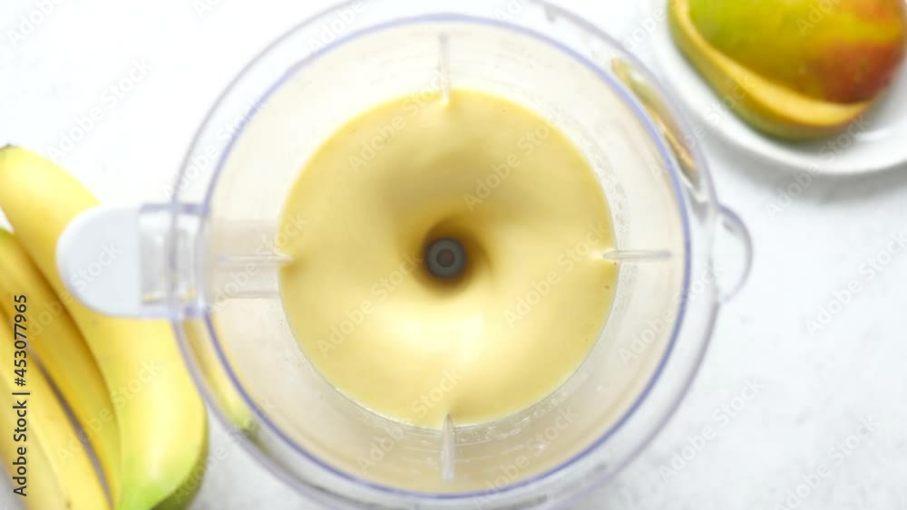 Top view yello tropical fruit smoothie mixing in blender. Mango banana ...
