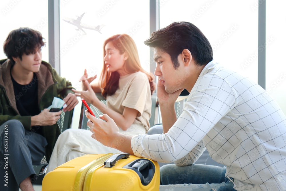 Asian young man holding and looking at mobile phone while waiting ...