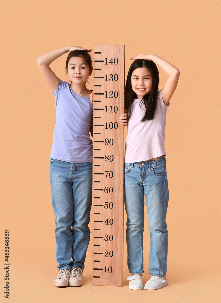 Cute little sisters measuring height on color background Stock Photo ...