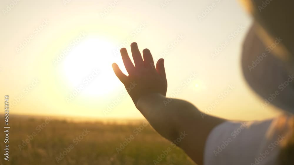 child's hand stretches out to rays of sun during sunset, beautiful ...