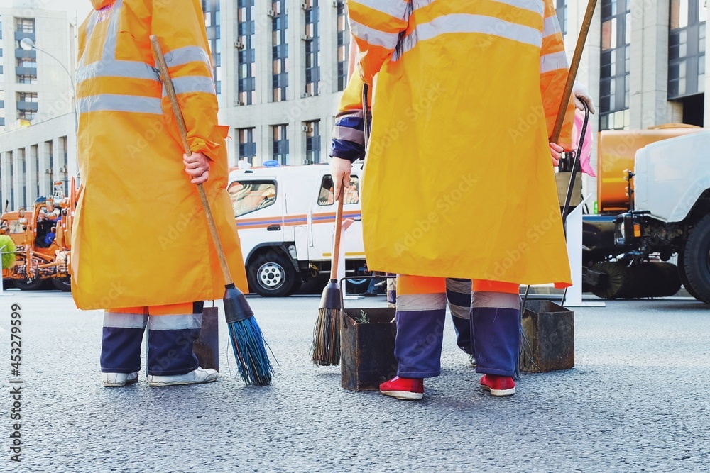 The back view close up of municipal workers in orange uniform sweep ...