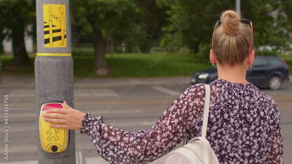 Female pedestrian presses a traffic light button to cross the road. The ...
