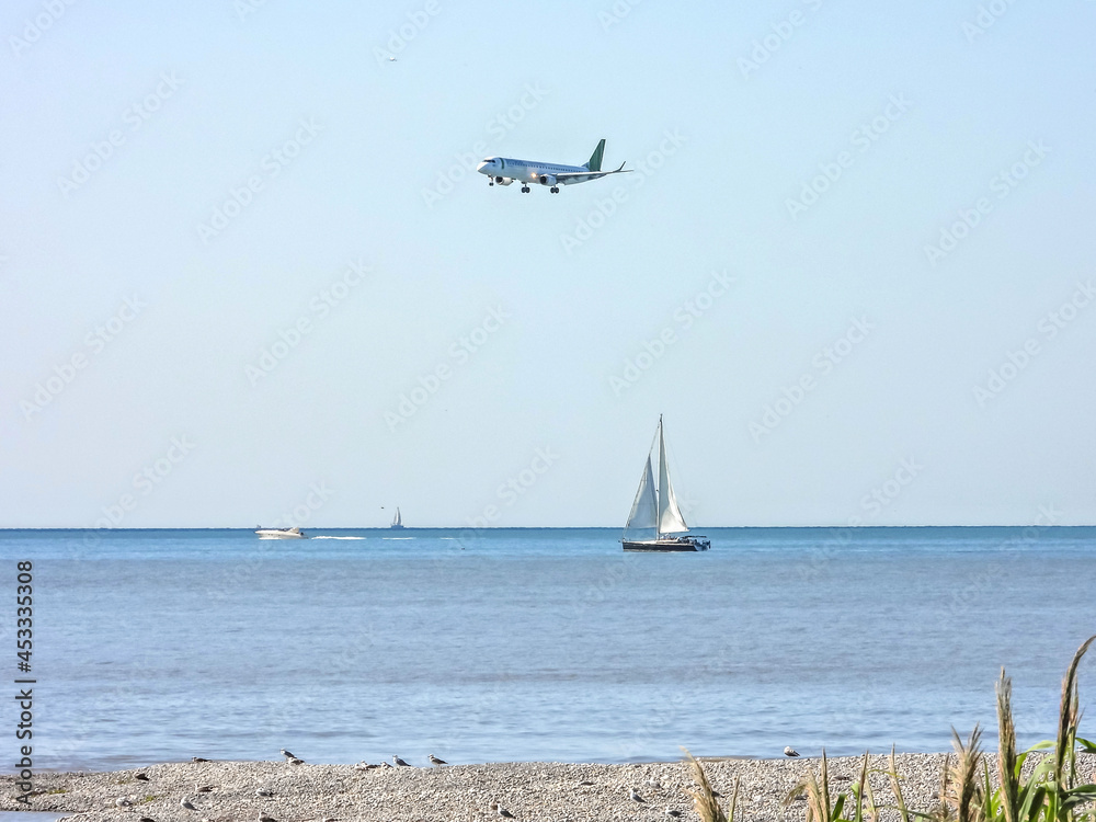 Avion en approche survolant la mer et un voilier Stock Photo | Adobe Stock