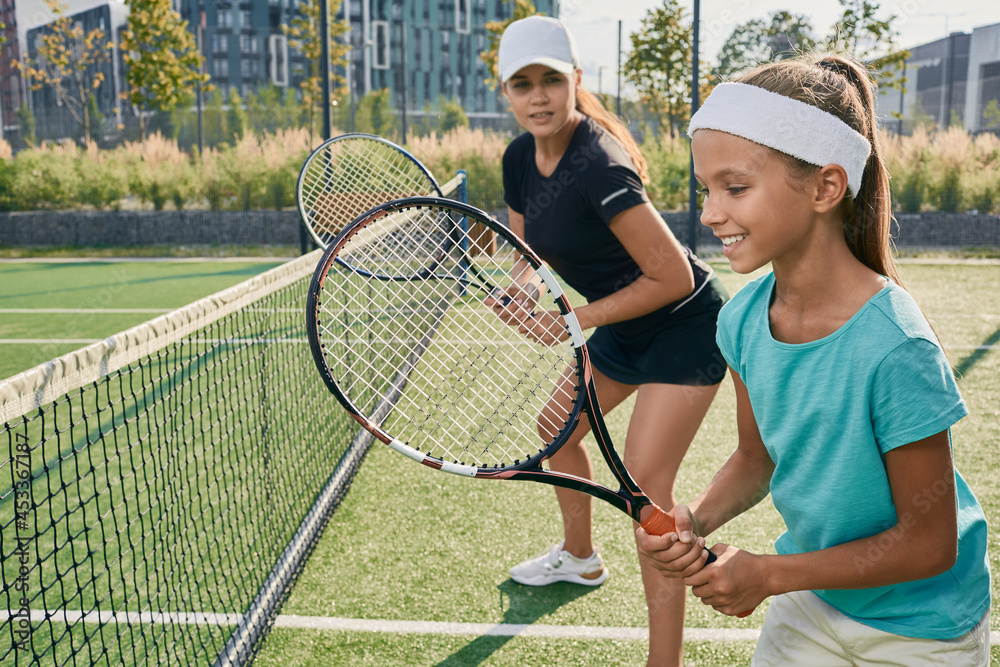Positive little girl holding a racket while learning to play tennis ...