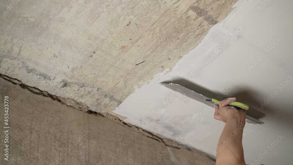 Hand with a putty knife and putty, apply mastic to the ceiling to level ...