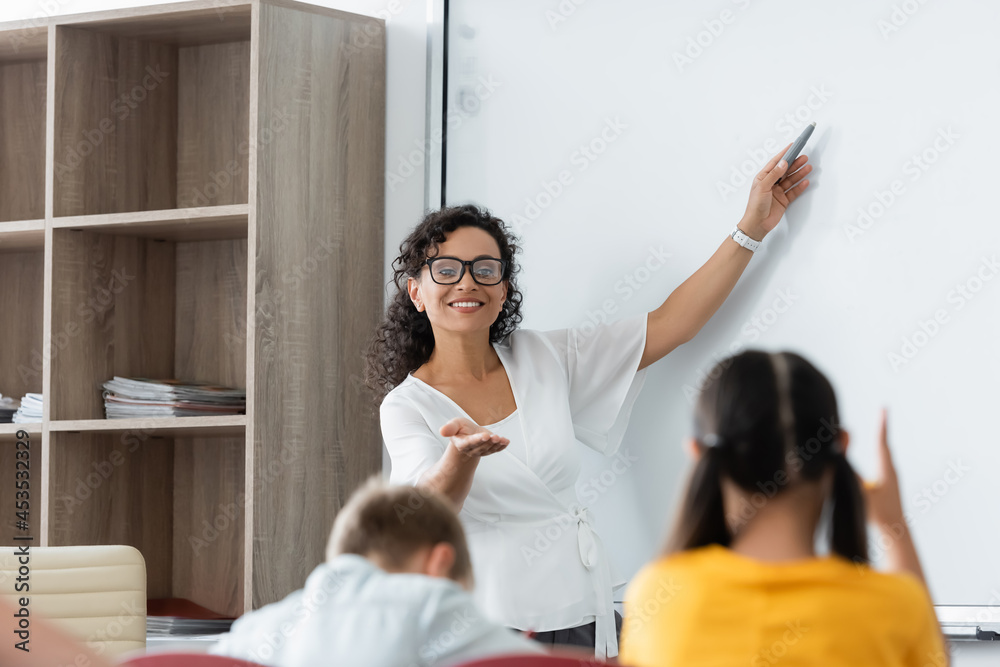 smiling african american teacher pointing at erase board and pupils ...