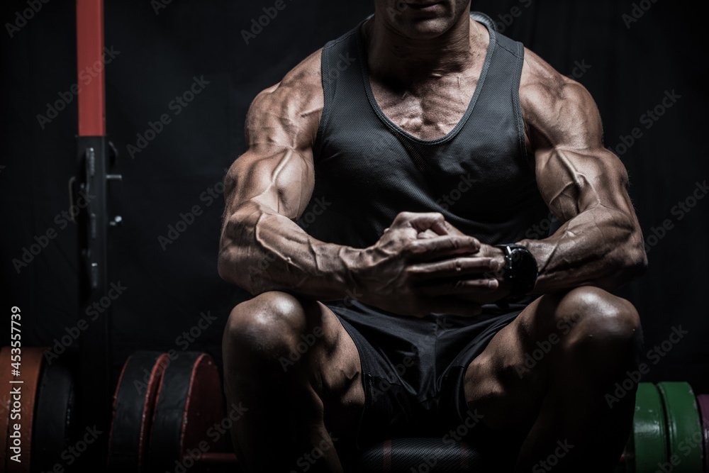 Very muscular bodybuilder man with veins on the body sitting in dim ...