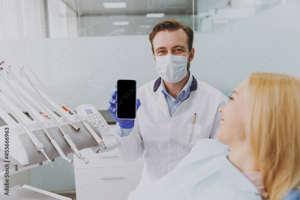 Young friendly man dentist show mobile cell phone with blank screen ...