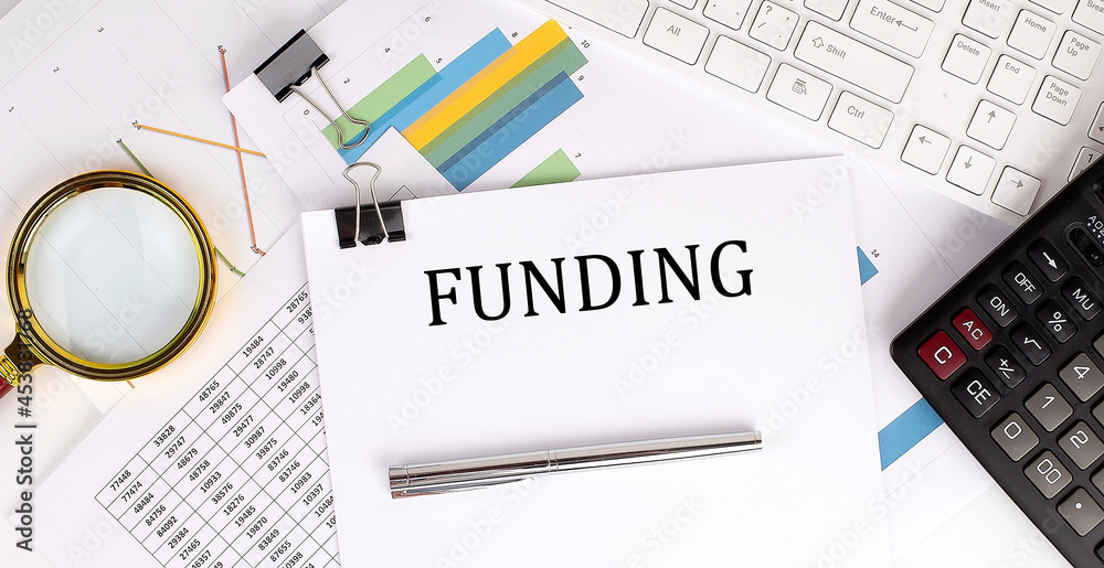 FUNDING text on the white paper on the light background with charts ...