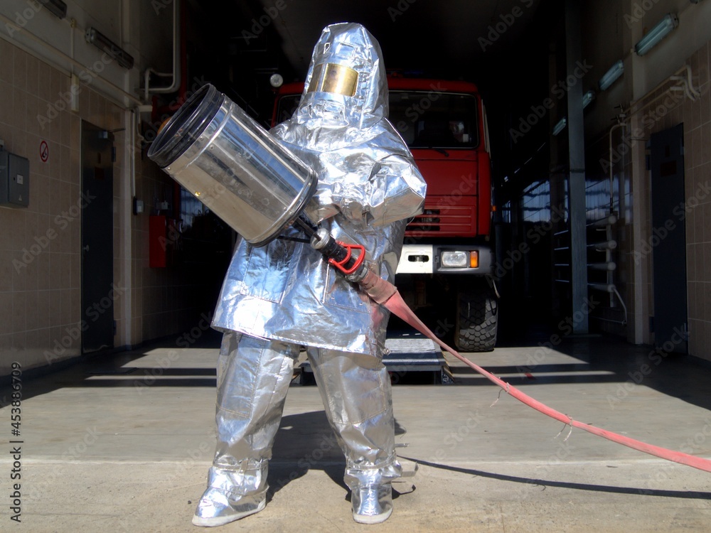 A firefighter in a shiny heat-reflecting suit. The firefighter has a ...