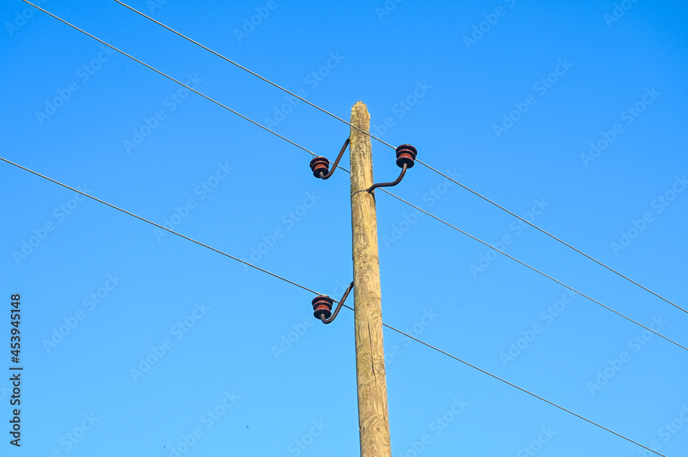 Wooden pillar with strain insulator and electricity cables hanging on ...