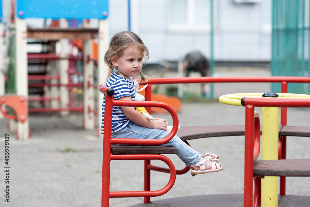 A cute little girl is whirling alone on a red merry-go-round in a ...