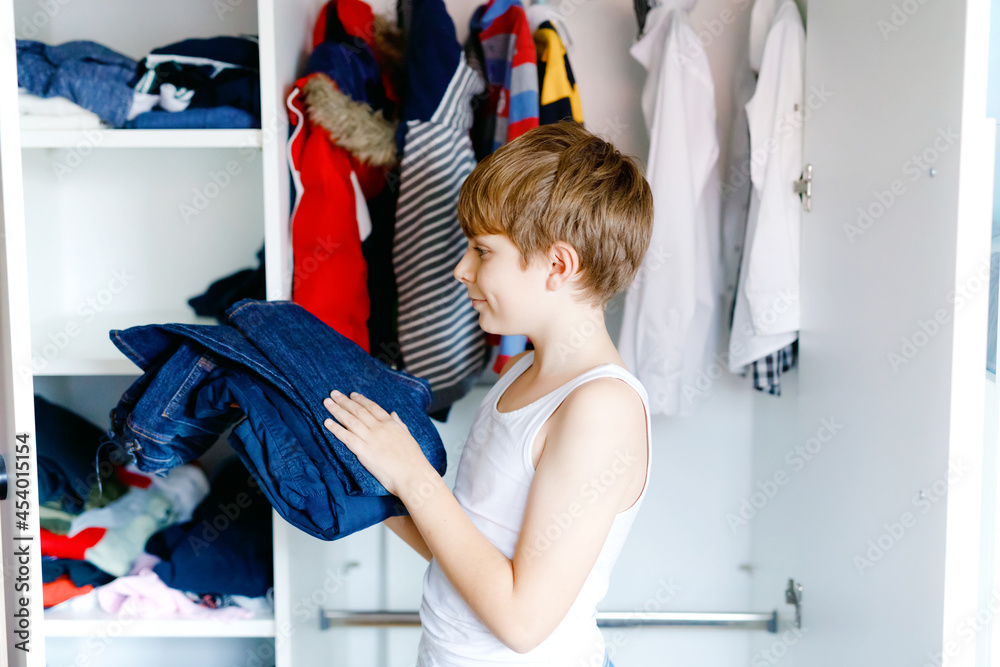 Foto de School kid boy standing by wardrobe with clothes. Child making decision for school jeans ...